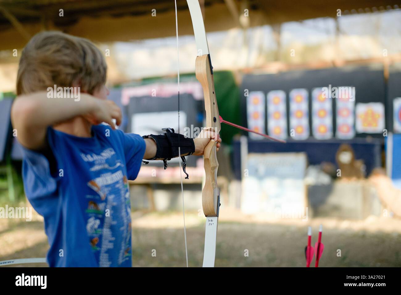 Child practicing archery, aiming a bow with arrows at a target in an ...