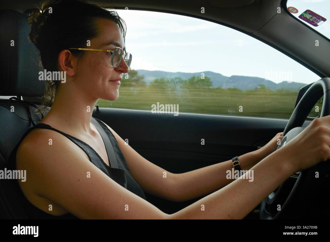 Young woman driving a car through scenic countryside with mountains ...