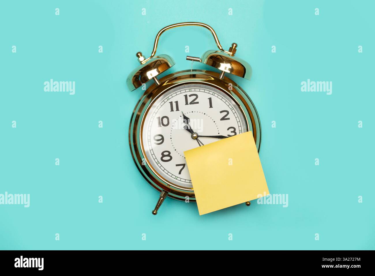 A blank yellow sticky note glued on the face of a bell alarm clock on a ...