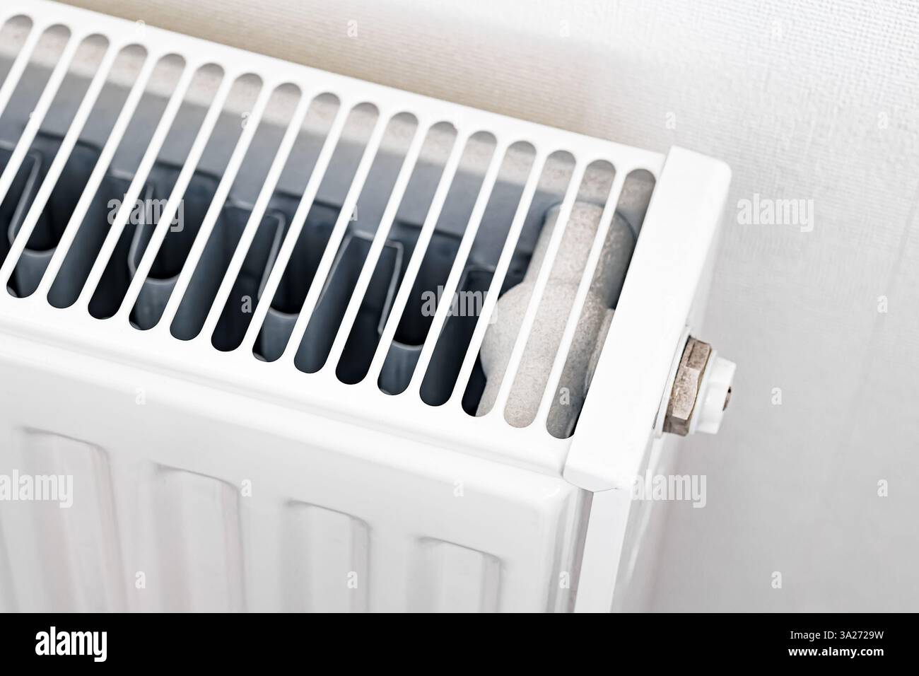 Close-up of an old white radiator with a heating valve and metal pipes ...