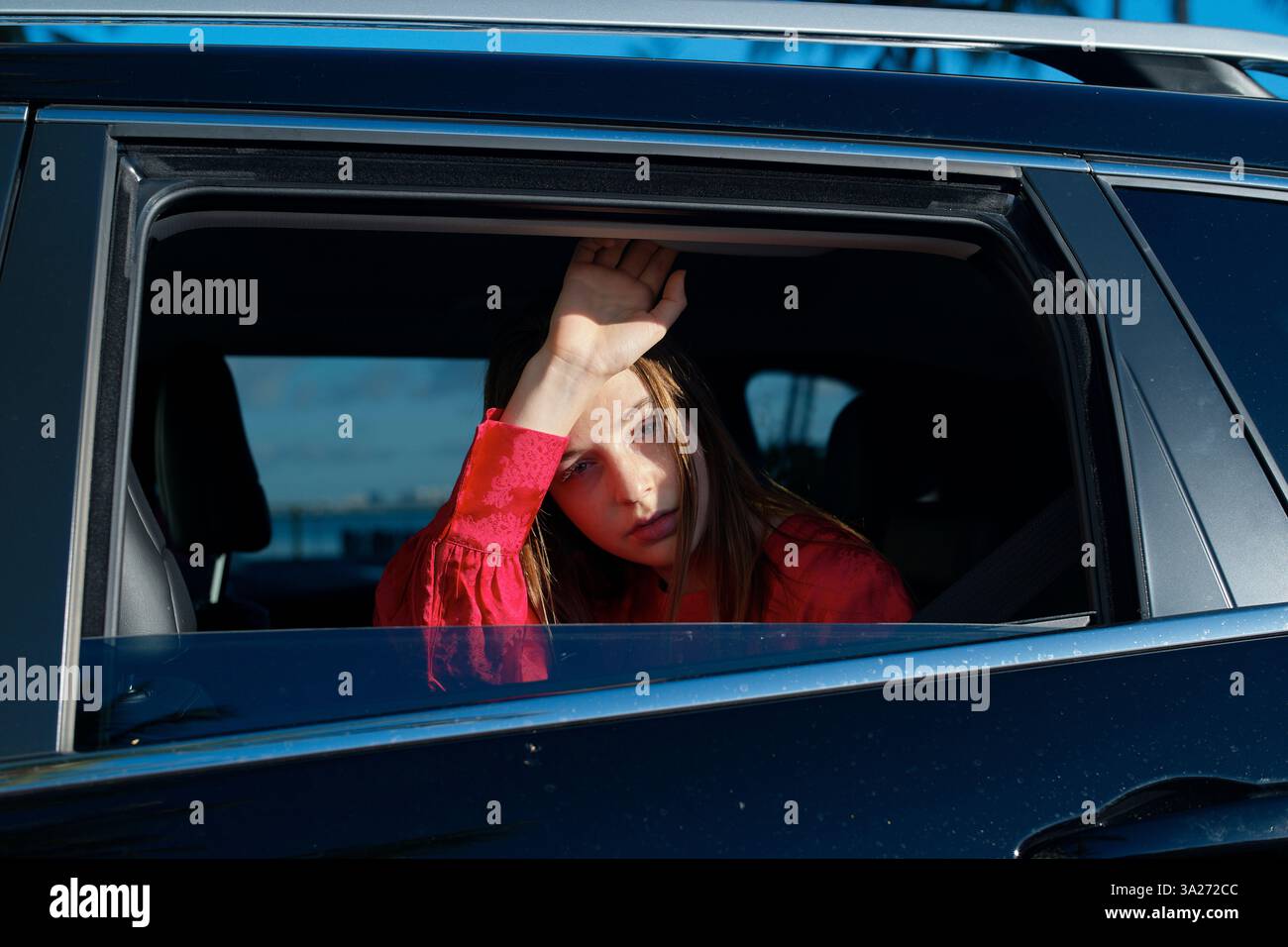 Woman in a red top looks out of a car window shielding her eyes from ...