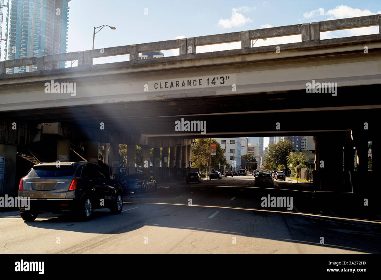 Urban street with cars driving under a concrete bridge on a sunny day ...