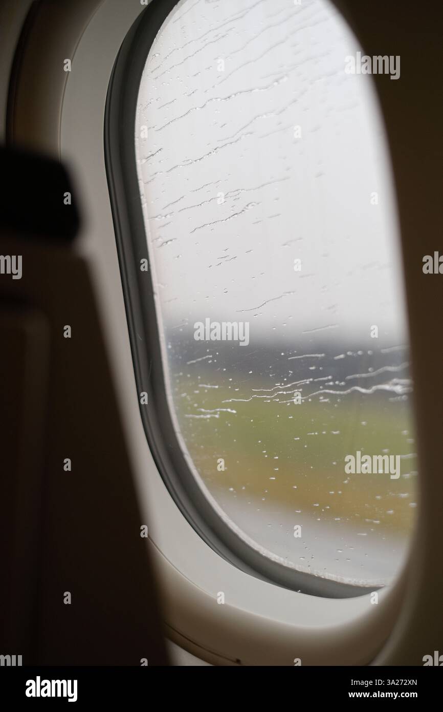 Rainy airplane window view with raindrops and dull outside scenery ...