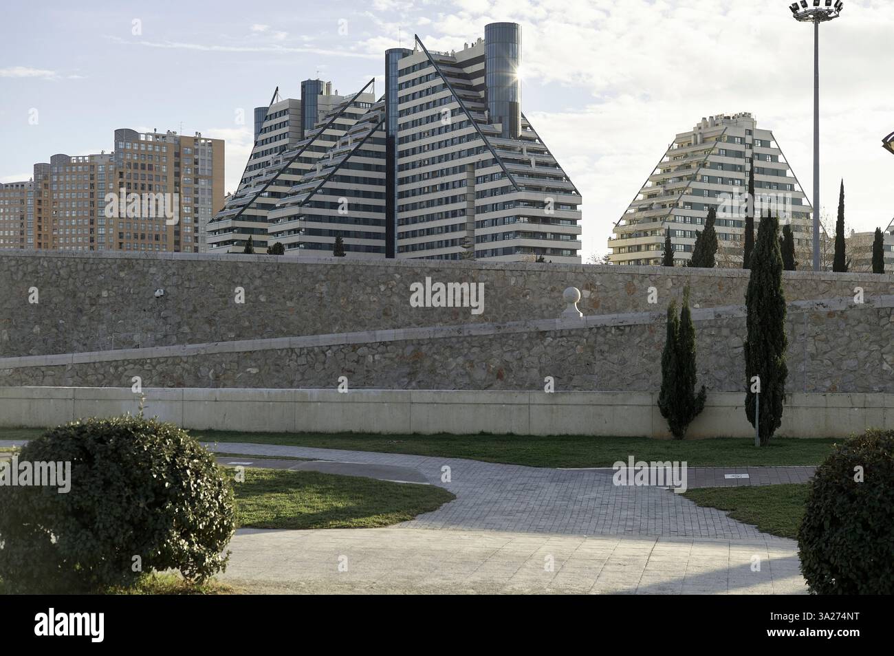 Modern triangular buildings with stone wall, trees, and path in urban ...