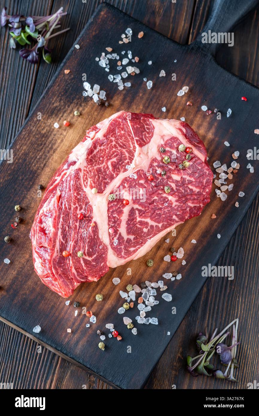 Thick, marbled ribeye steak resting on a rustic board, seasoned with ...
