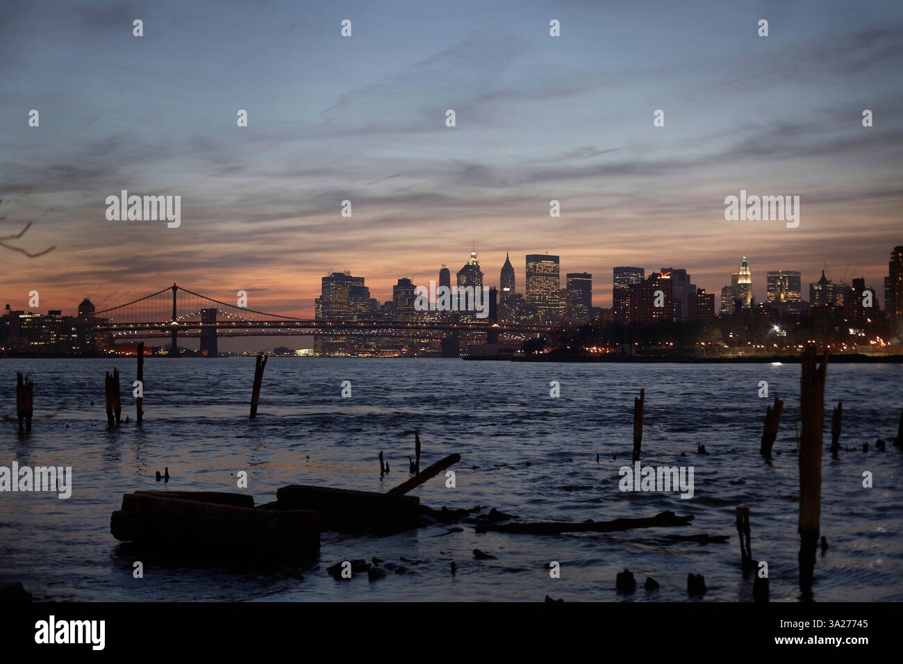 Brooklyn Bridge and New York City skyline at dusk over a calm river ...