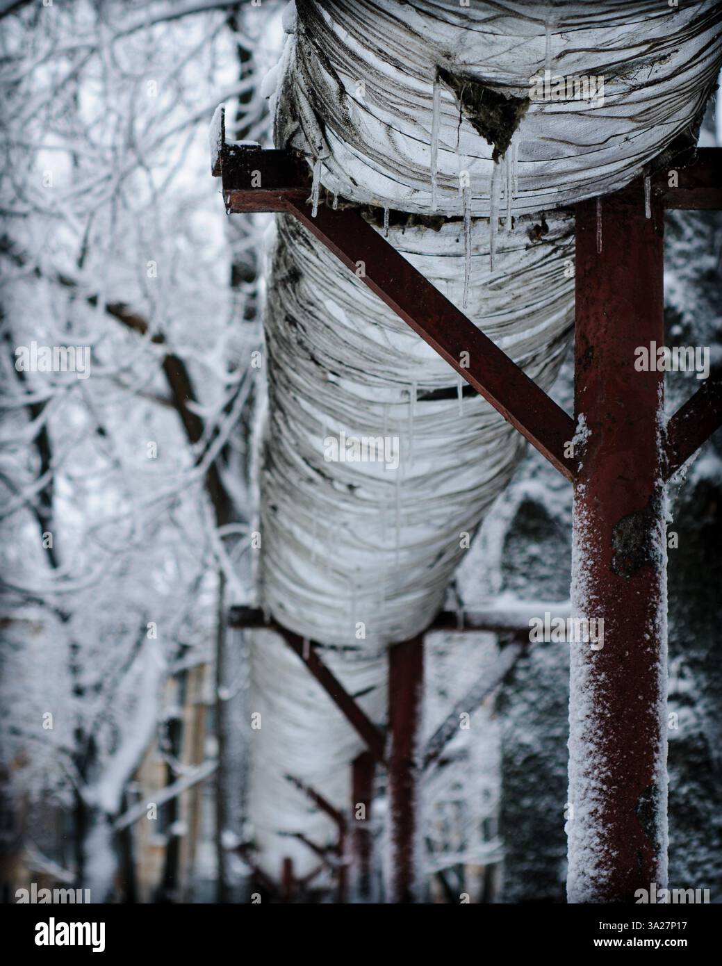 A winter urban scene featuring an old, insulated heating pipe covered ...