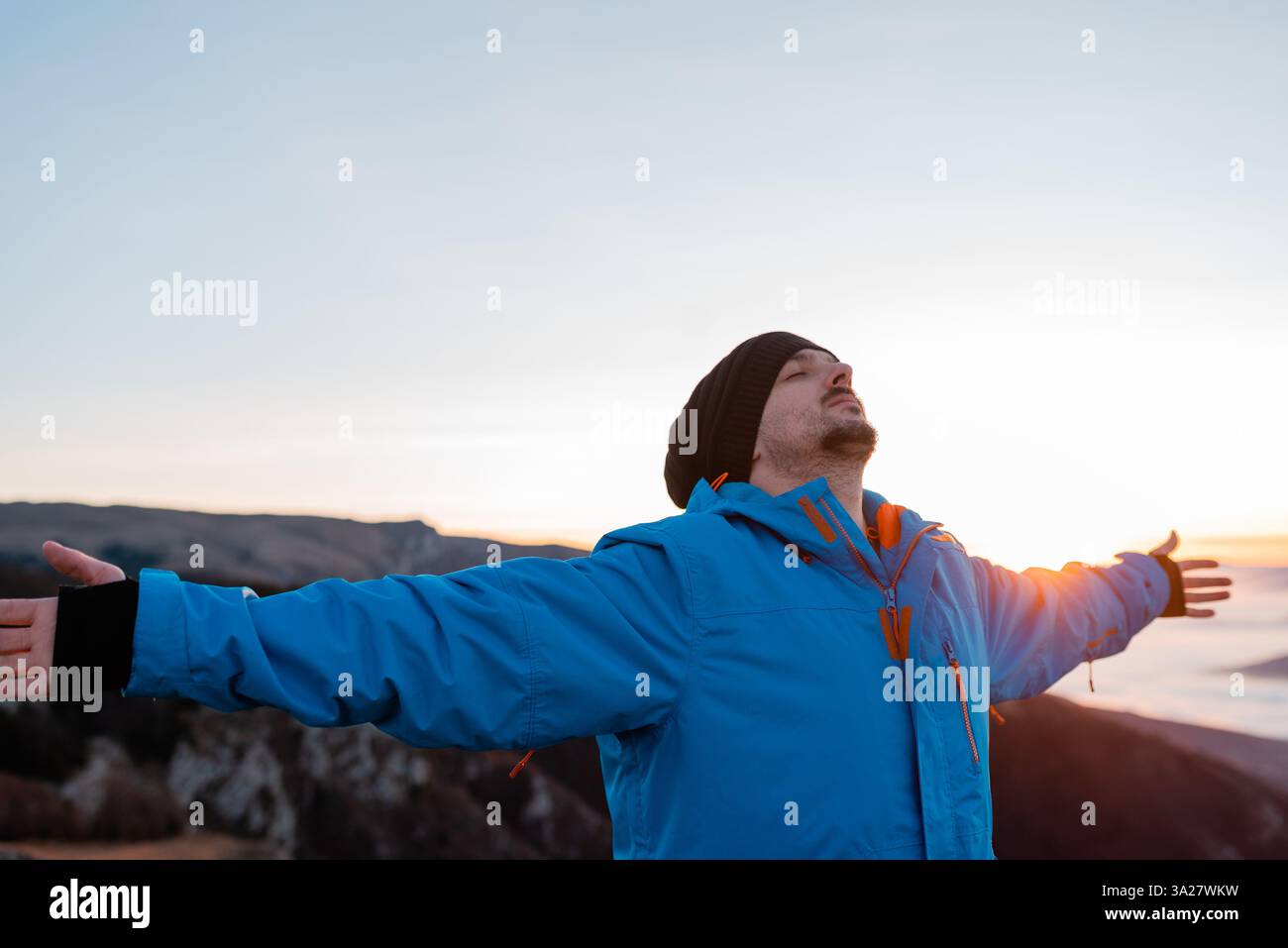 A carefree relaxing man deep breathing with arms outstretched and eyes ...