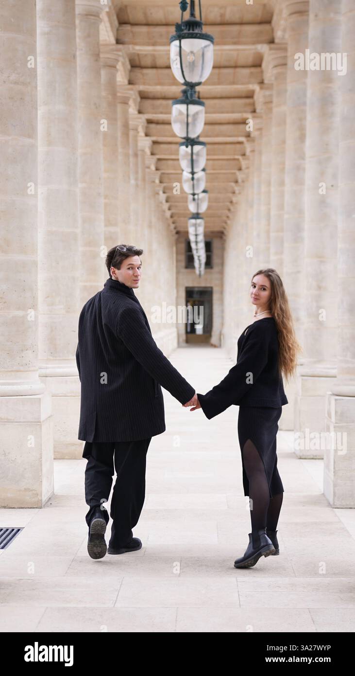 A fashionable couple dressed in elegant black outfits walks hand in ...
