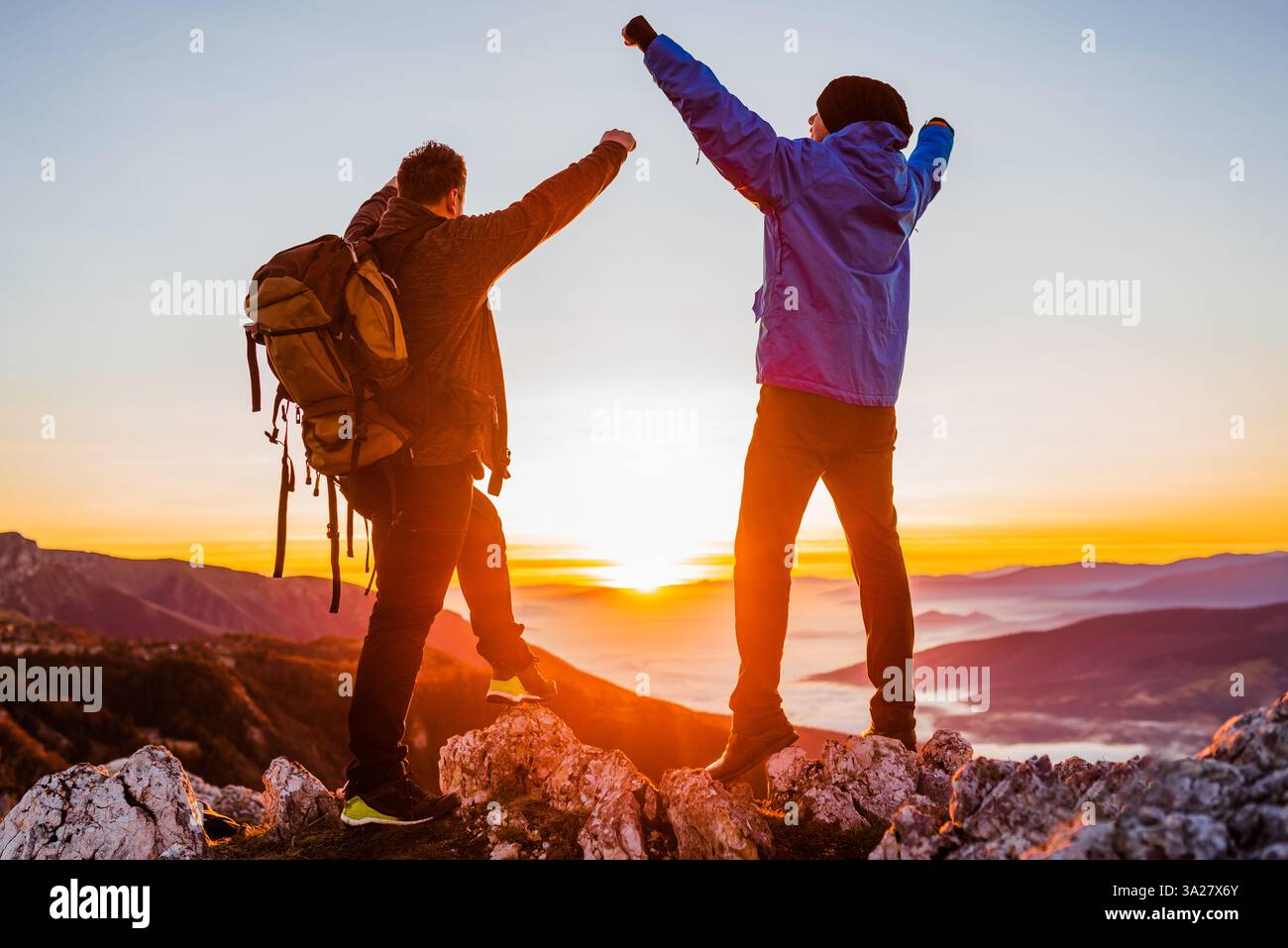 Two happy friends hikers standing with arms up on the mountain top ...