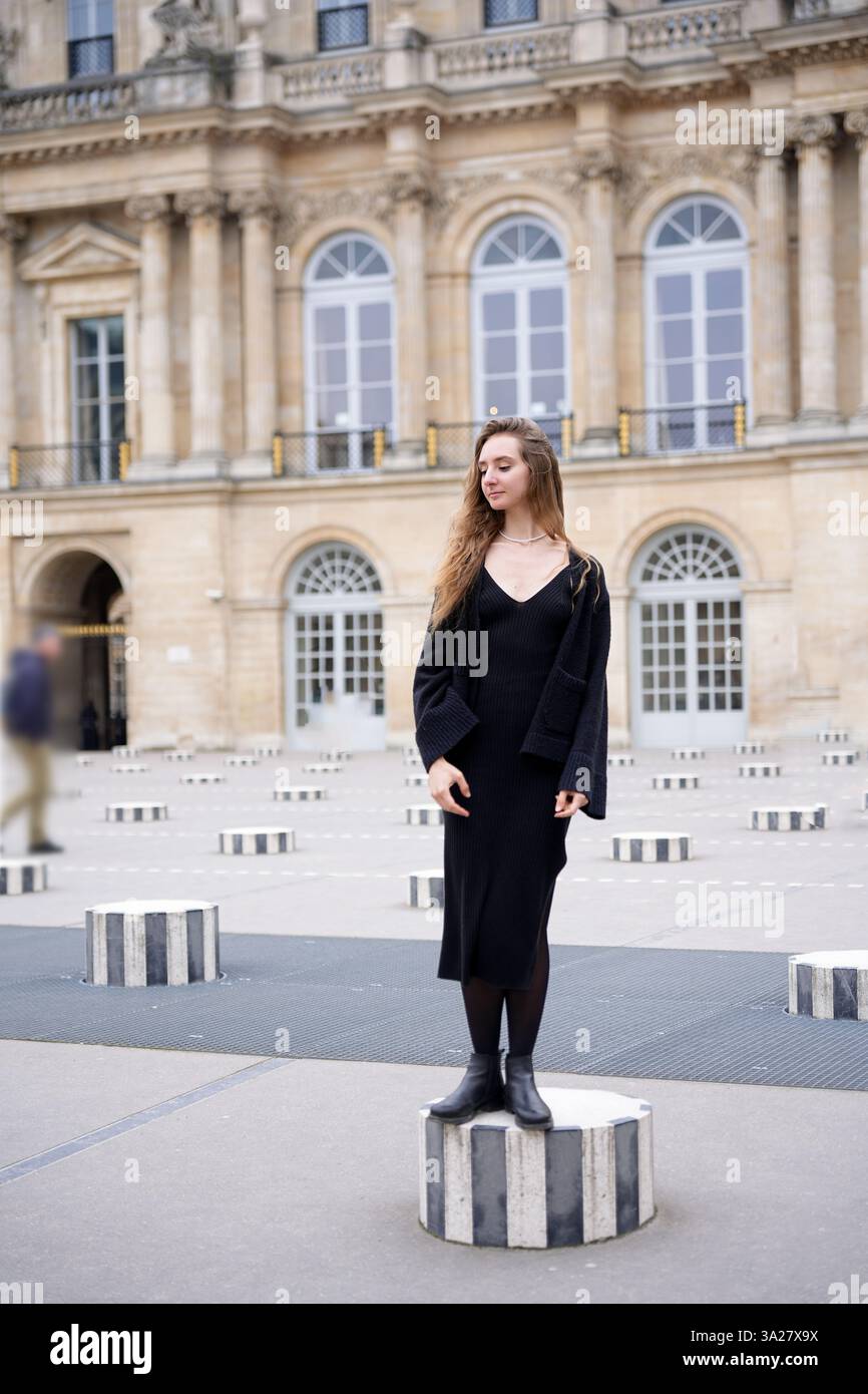 A stylish woman in a black dress and jacket poses gracefully on a ...