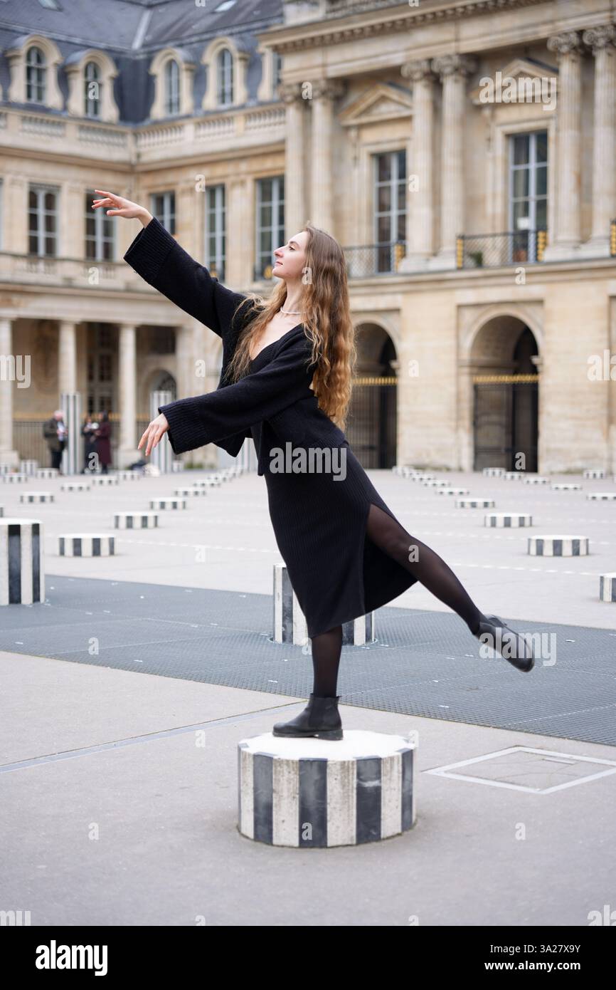 A stylish woman in a black outfit elegantly balances on a striped ...