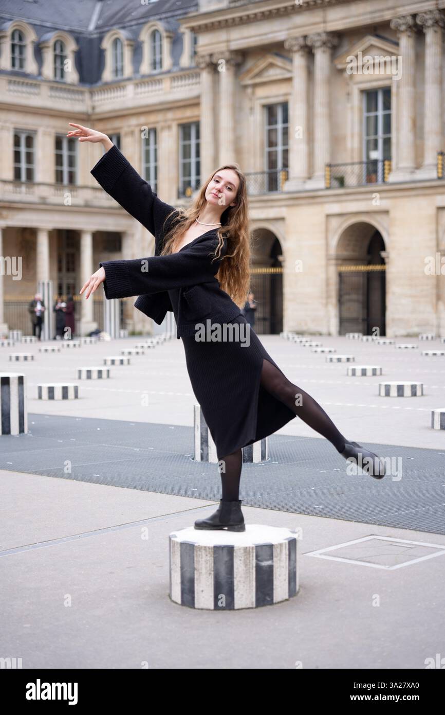 A stylish woman in a black outfit poses gracefully on a striped column ...