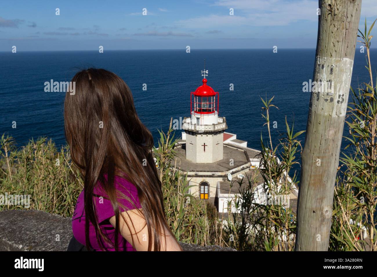 A woman with long brown hair gazes at a lighthouse perched on a cliff ...