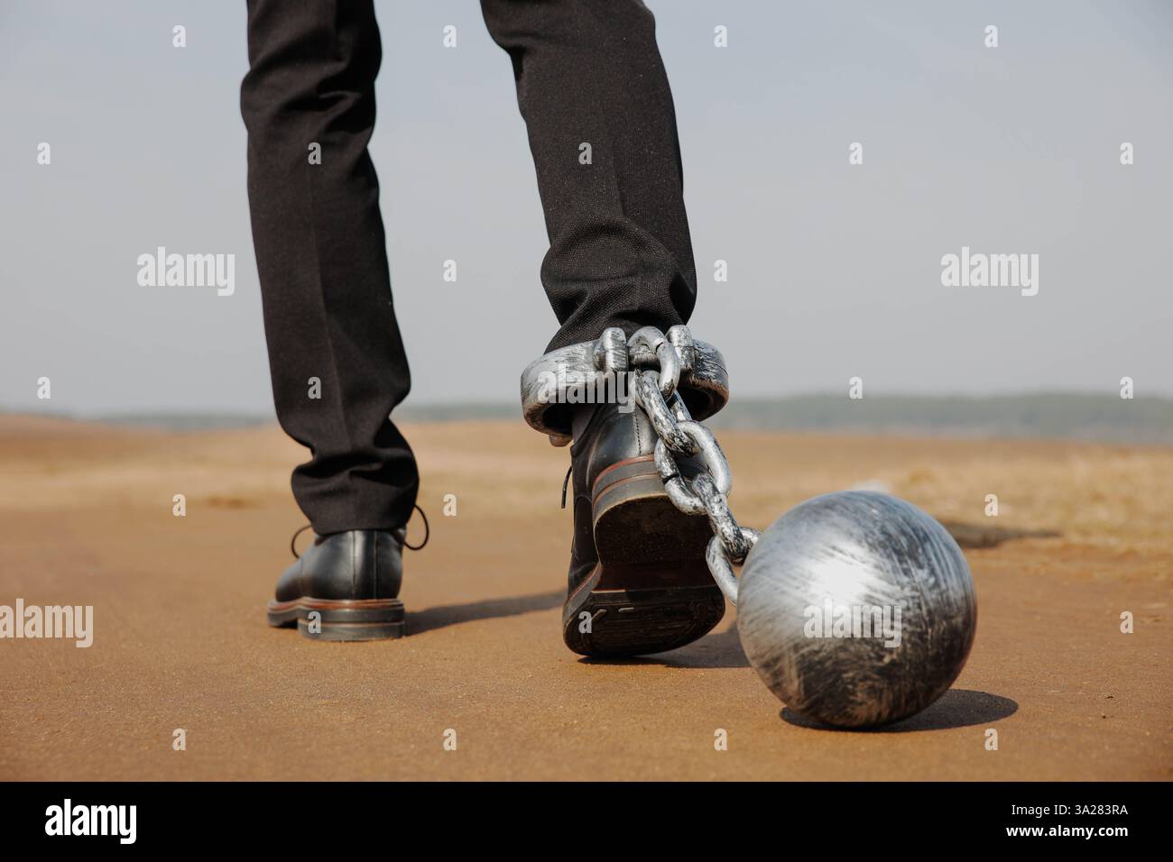 Tired businessman with iron shackles on his legs walks down the road ...