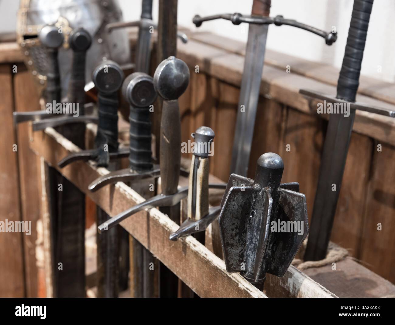 Various medieval swords and weapons are displayed in a wooden rack ...