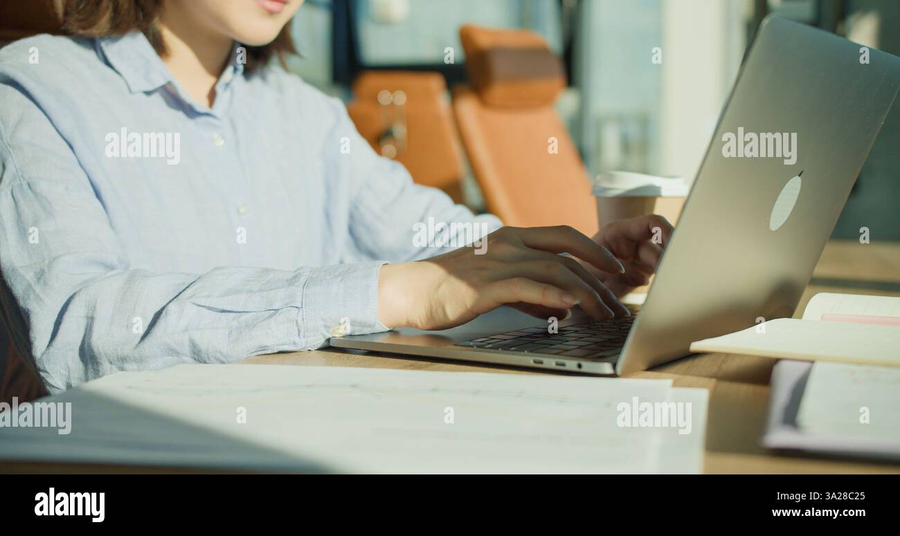 A close-up of hands typing on a laptop keyboard with charts, documents ...
