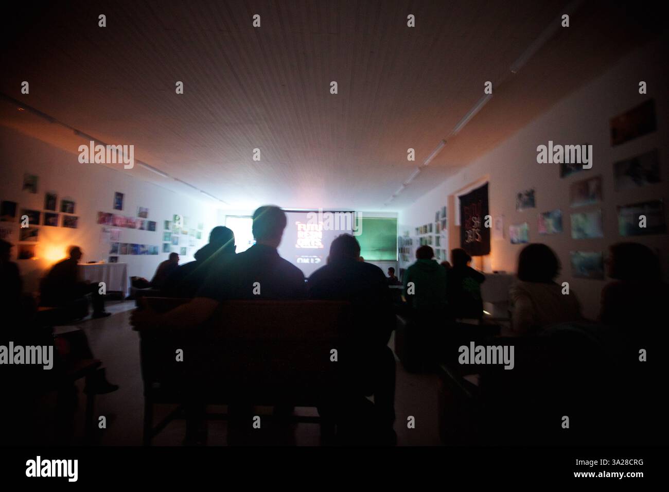 A dimly lit room with people seated, watching a presentation on a large ...