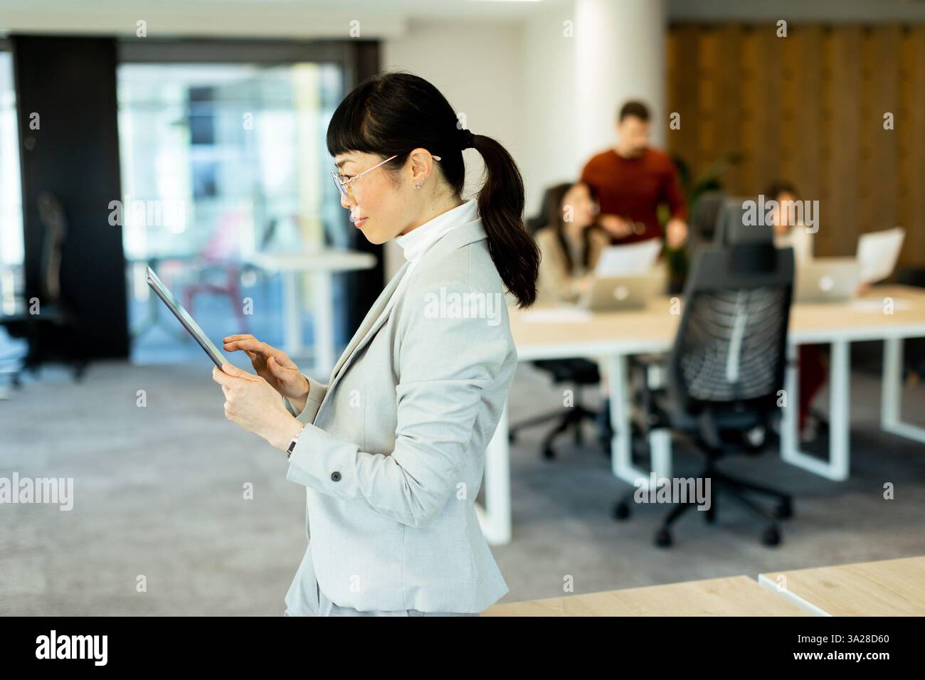 A focused Japanese woman in a suit reviews a document while colleagues ...