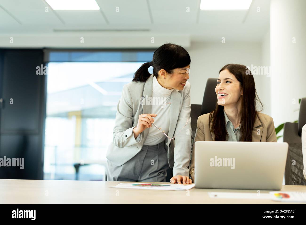 In a contemporary office setting, two women engage in a cheerful ...