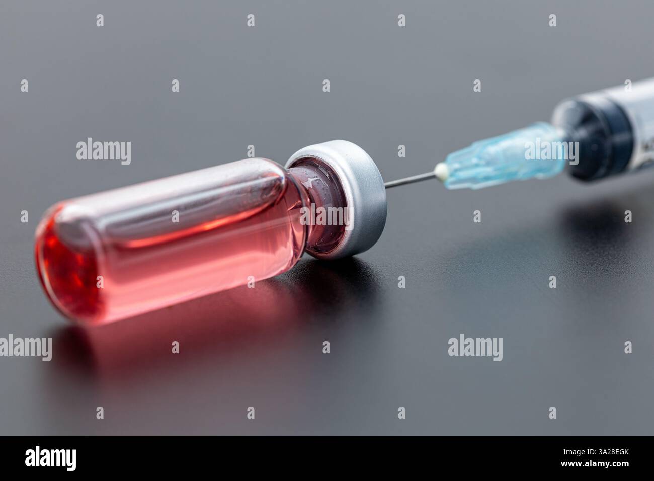 Syringe with red liquid on a black background representing medical ...