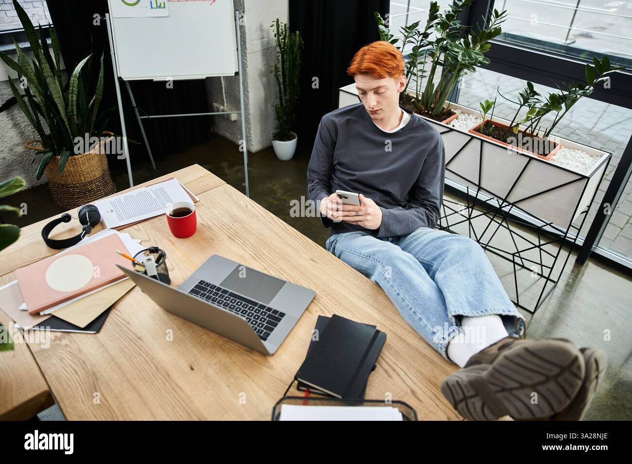 Focused young man with red hair engages with his smartphone amid office ...