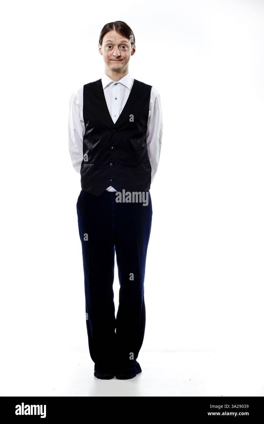 A person standing straight with a slight smile, wearing a formal outfit ...