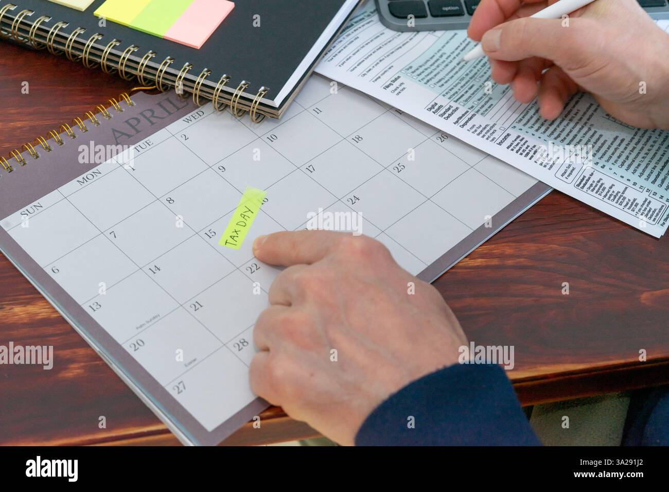 A person filling out a U.S. tax form, the hand is signaling the day of ...