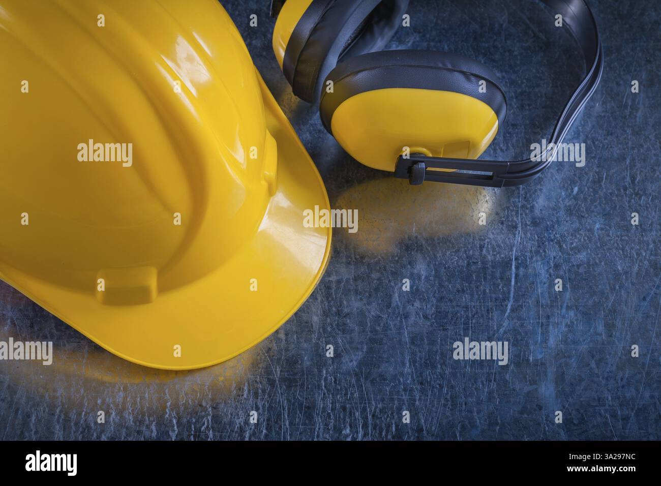 Safety yellow ear muffs and work helmet on scratched metallic ...