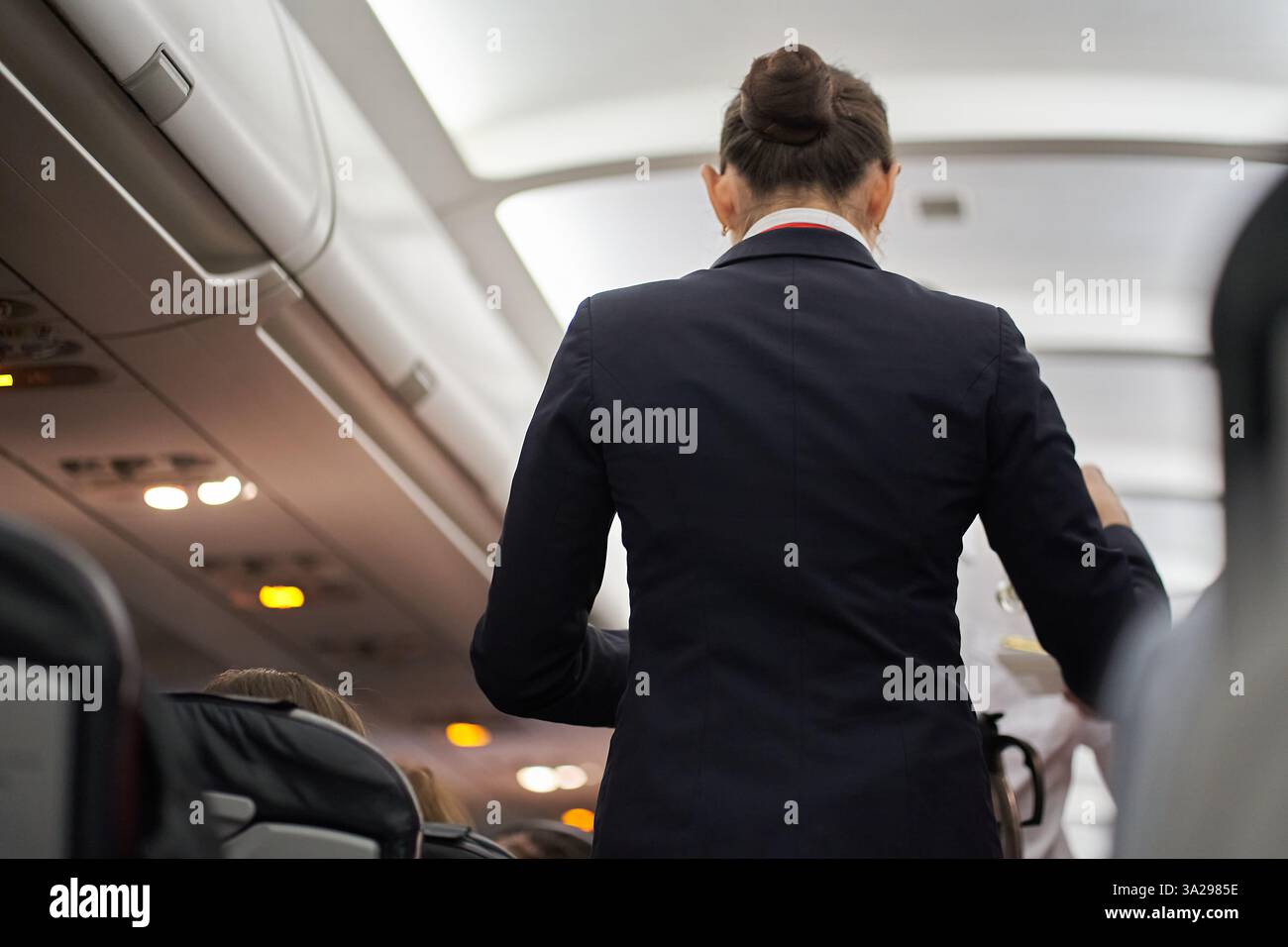 Rear view of a flight attendant in a black uniform on a plane with ...