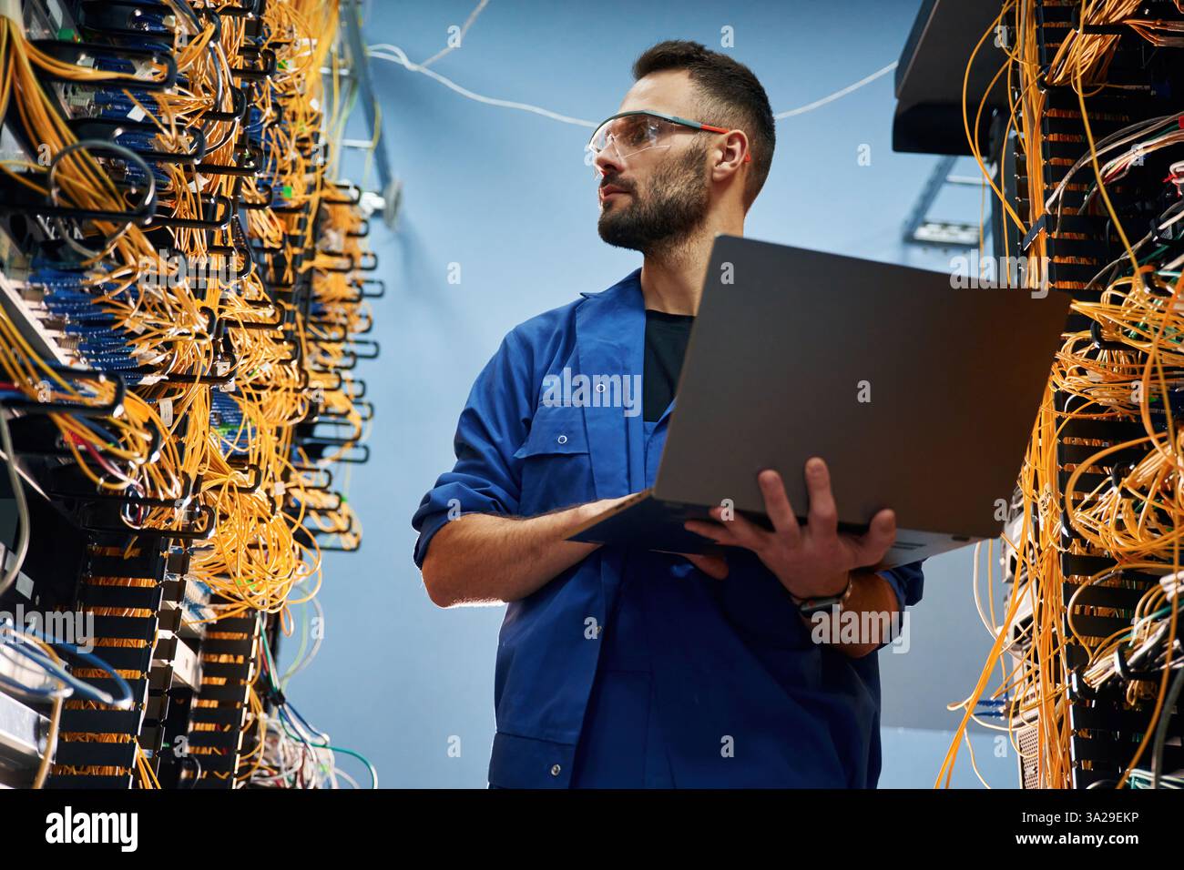 Holding laptop. Young man is working with internet equipment and wires ...