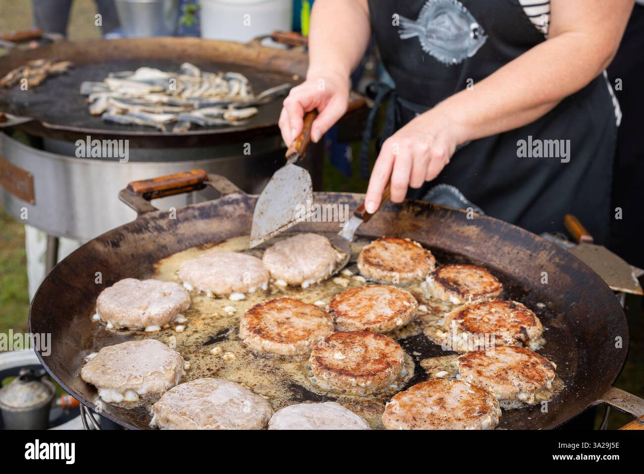 A large round grill is roasting fish patties. Fresh fish cutlet in a ...