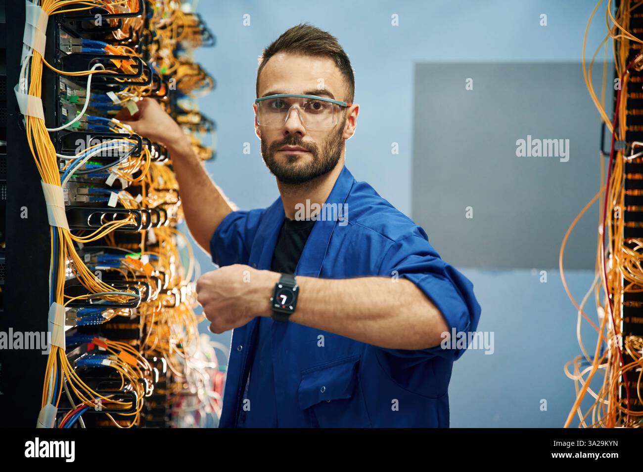 Showing watch. Young man is working with internet equipment and wires ...