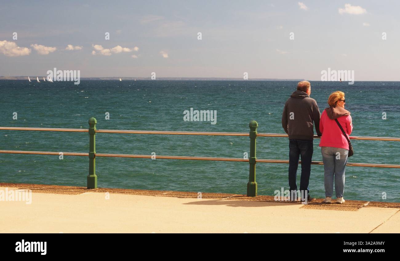 A middle aged couple, man and wife, leaning on the promenade railings ...