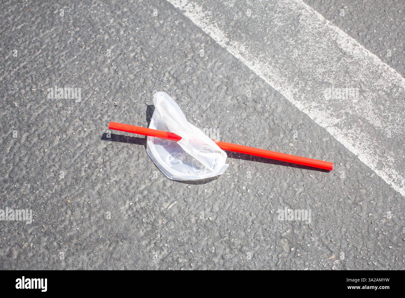 A view of trash on the pavement, featuring a plastic drink lid and ...