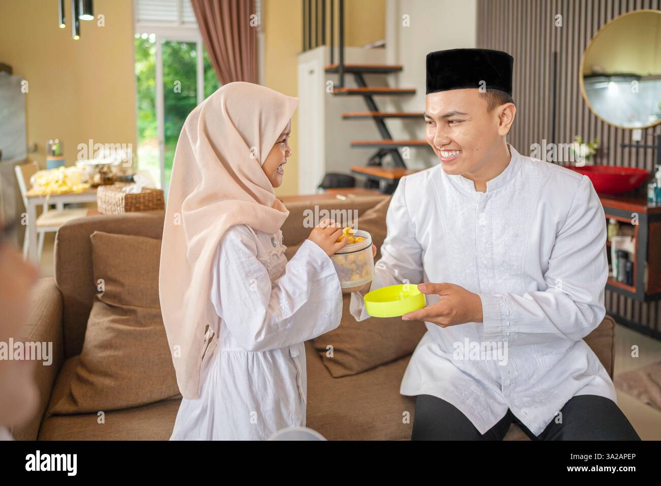 Portrait of the Indonesian Muslim father sharing a cake with his daughter while celebrating Eid ...