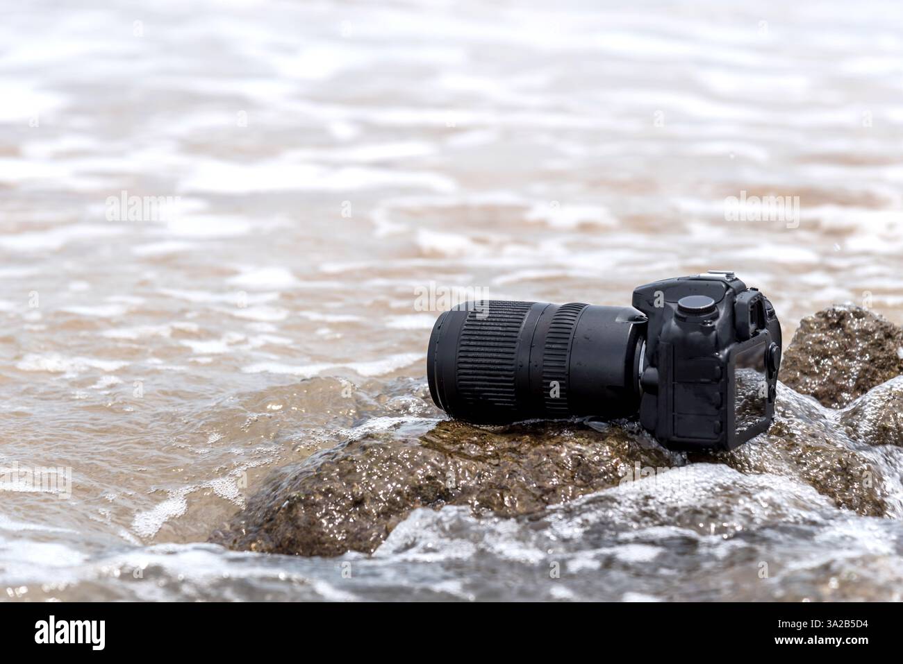 DSLR camera with telephoto lens wet from water sea wave at stone beach ...