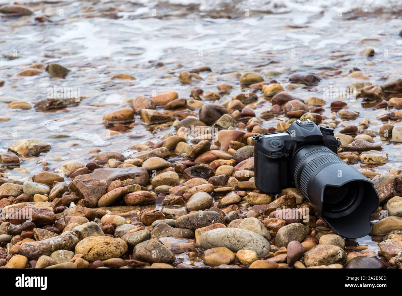 DSLR camera with telephoto lens wet from water sea wave at stone beach ...