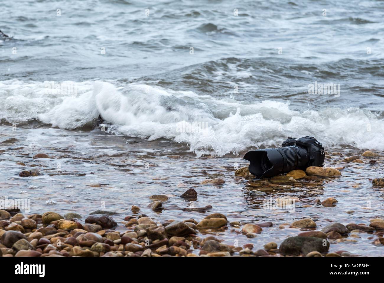 DSLR camera with telephoto lens wet from water sea wave at stone beach ...