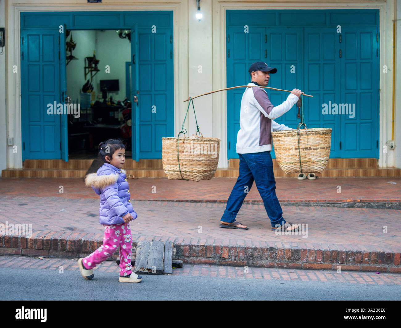 Man carrying baskets with his daughter on a bamboo pole in a street ...