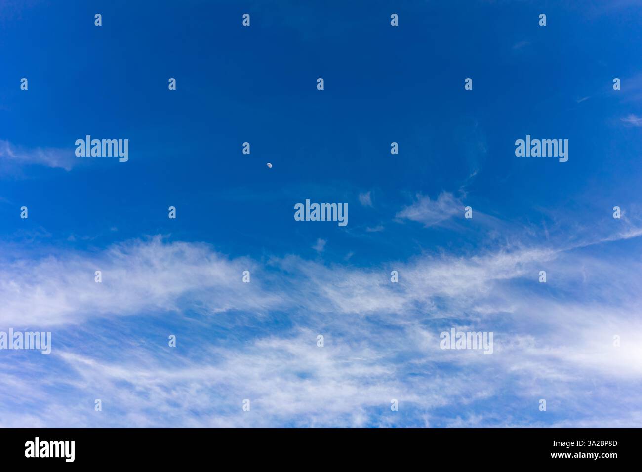 A vast blue sky filled with wispy white clouds and a faint crescent ...