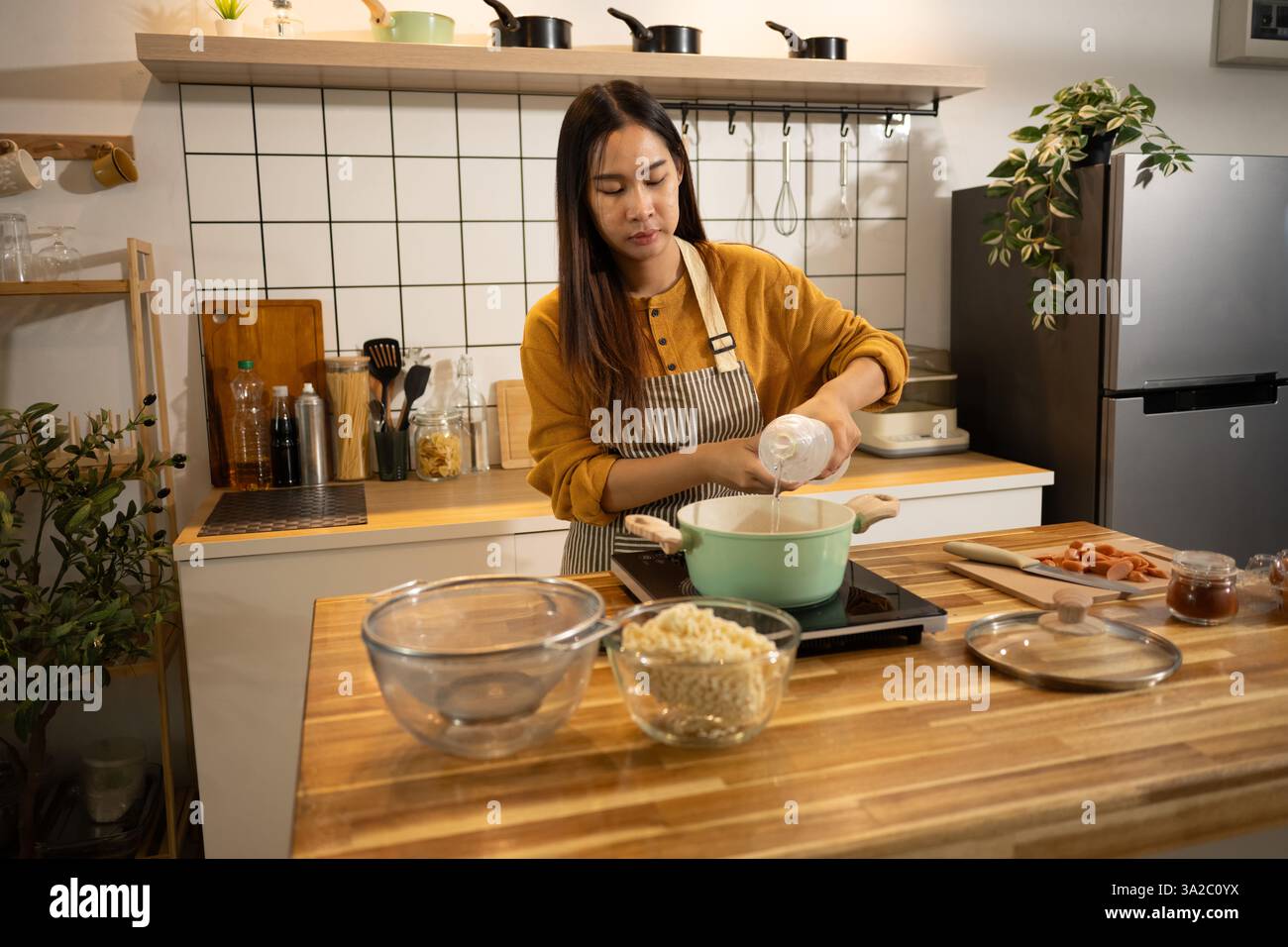 Young woman wearing apron adding water to a pot, getting ready to cook ...