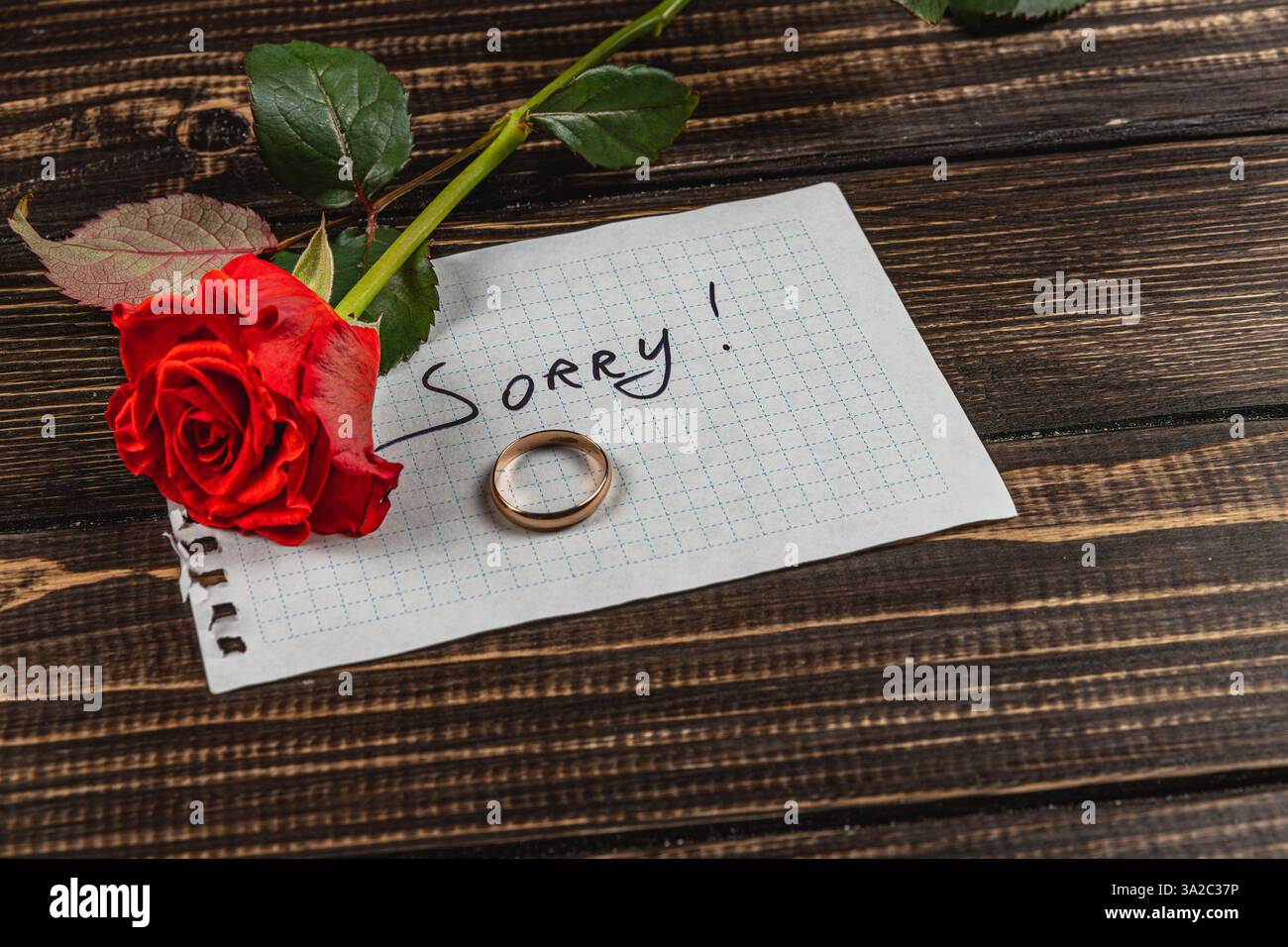 A wilted red rose lies next to a gold ring and a handwritten note that ...