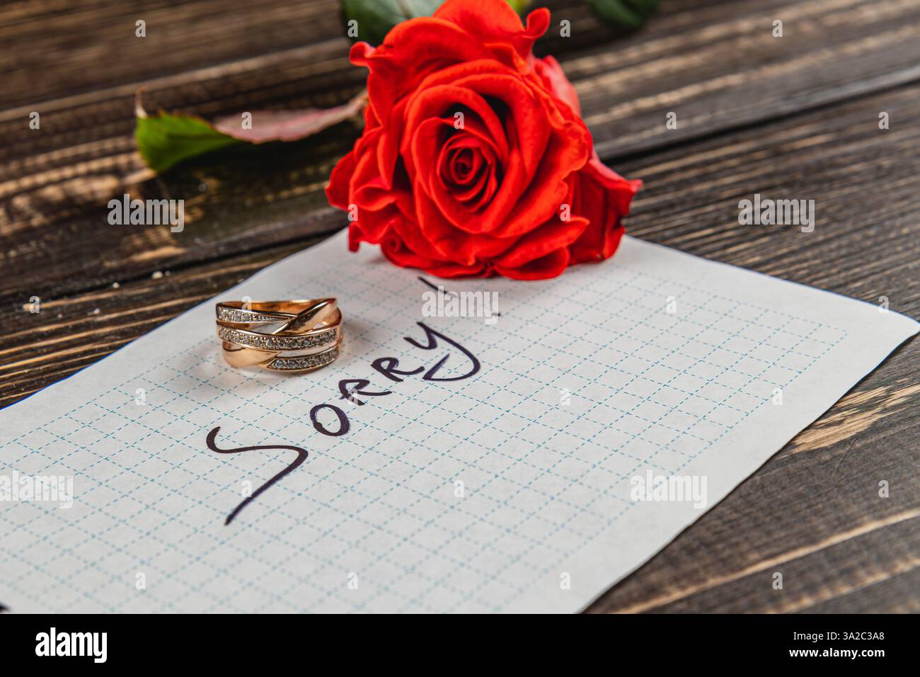 A note reading sorry is placed beside two wedding rings and a red rose ...