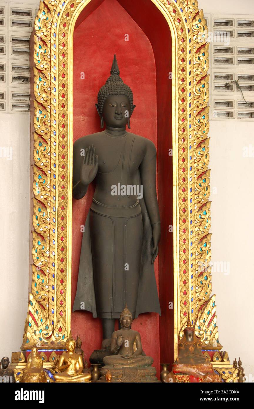 Black Buddha statue in Bangkok temple, framed by ornate golden patterns ...