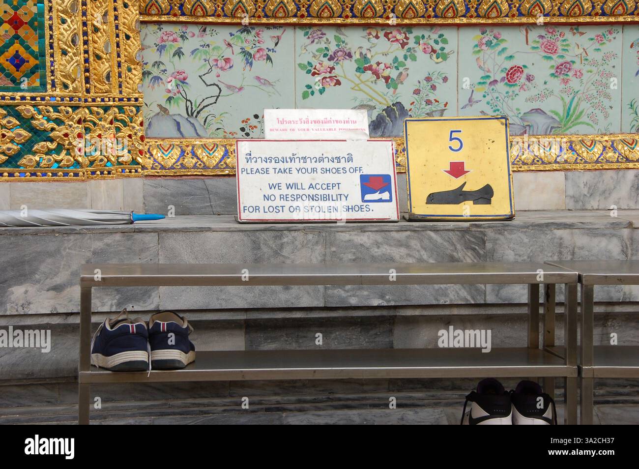 Shoe rack at a Thai temple entrance with signs instructing visitors to ...