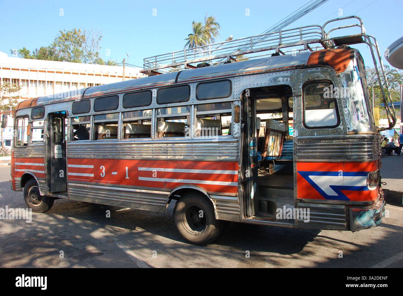 Vintage red and silver local bus in Surat Thani, Thailand, with open windows and metal roof rack ...
