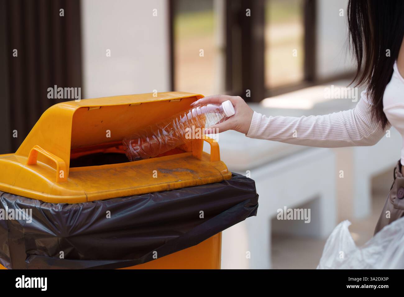 Individual recycling plastic bottles in a yellow bin, promoting ...