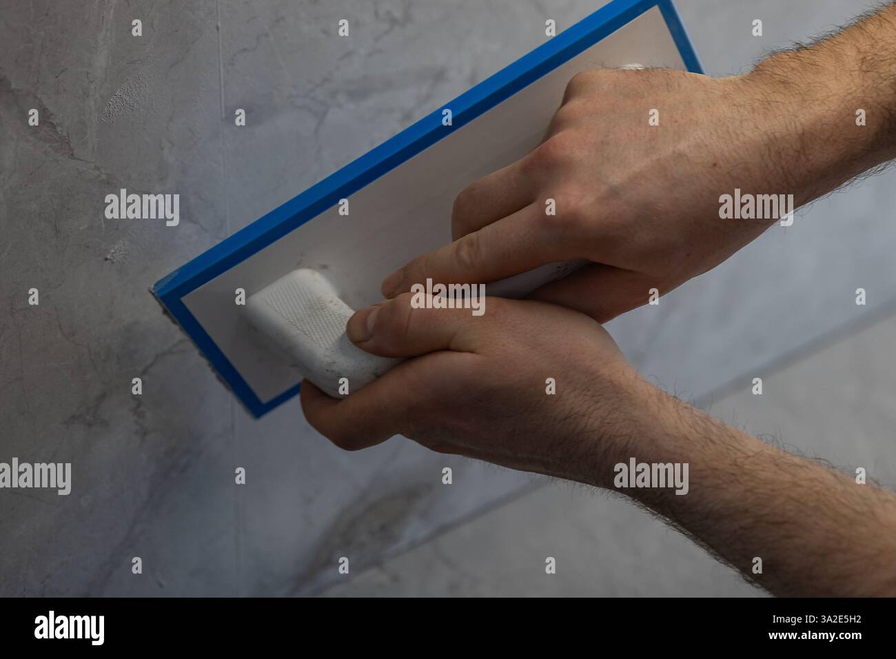 Worker applying grout on ceramic tiles using a rubber float during wall ...