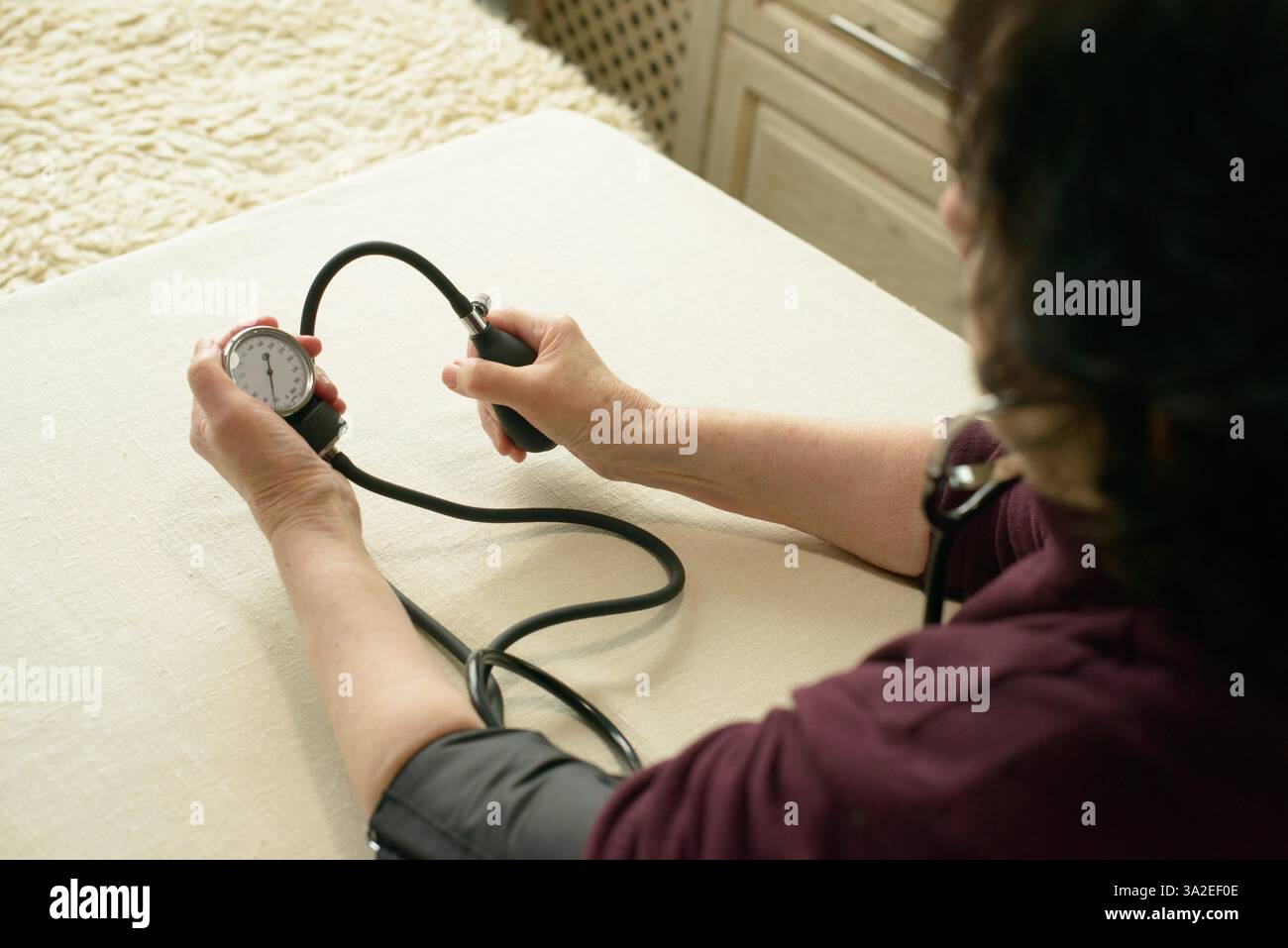 A senior woman using a manual blood pressure cuff and gauge in a home ...